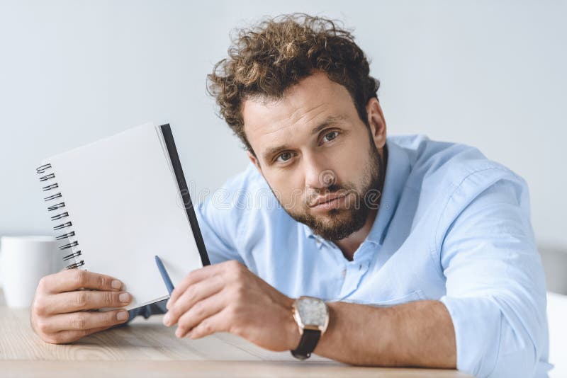 Businessman Sitting at Workplace and Pointing at Blank Notebook in Hand ...