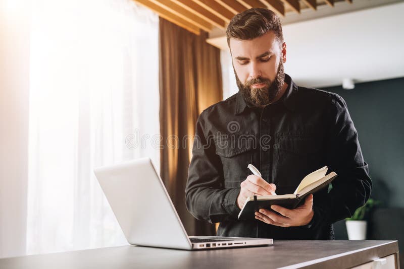 Businessman is Standing by Computer, Making Notes in Notebook. Man ...
