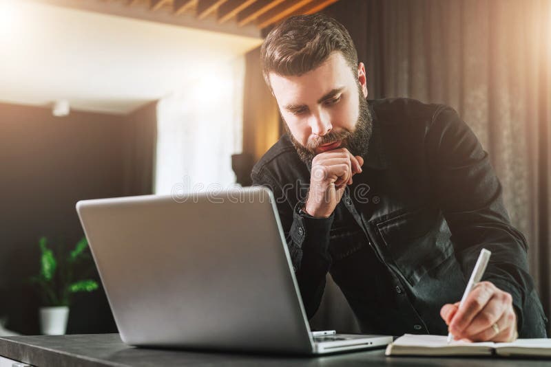 Businessman is Standing Near Computer, Working on Laptop, Making Notes ...