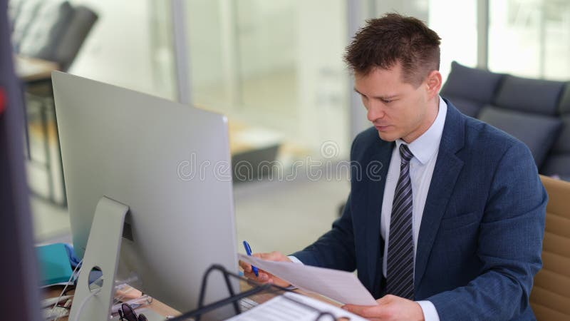 Businessman Studying Paper Document in Front of Computer in Office ...