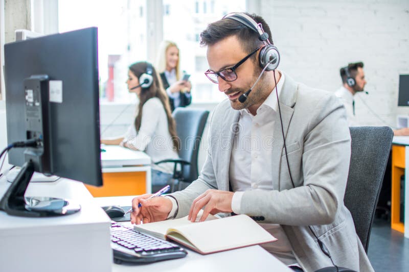 Businessman Taking Notes while Talking with Customer Using Headphones ...