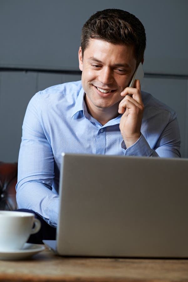 Businessman Talking on Mobile Phone Working on Laptop in Internet Cafe ...