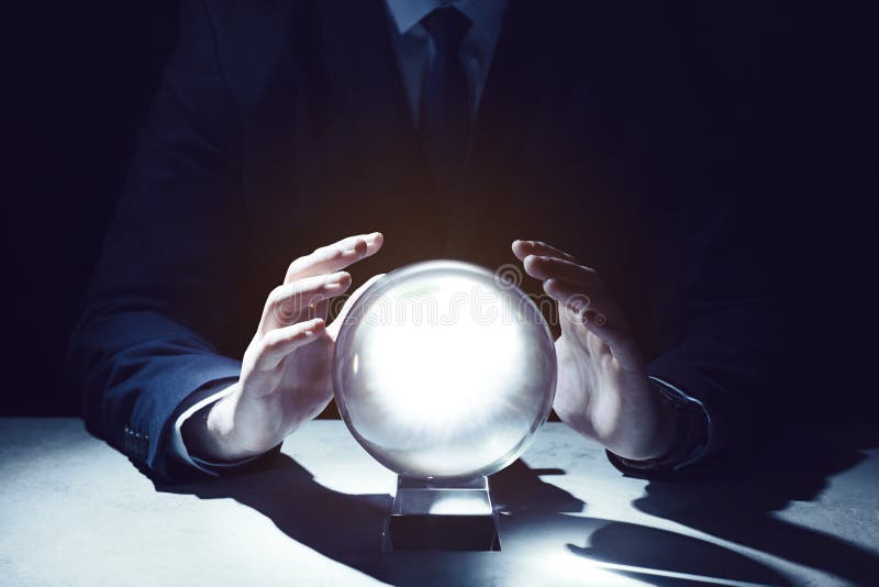 Businessman Using Crystal Ball To Predict Future At Table In Darkness