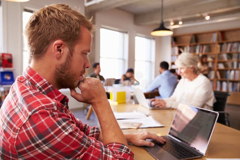 Businessman Using Laptop at Desk in Busy Office Stock Photo - Image of ...