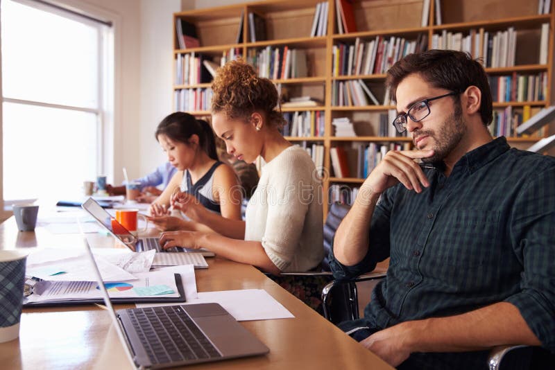 Businessman Using Laptop at Desk in Busy Office Stock Photo - Image of ...