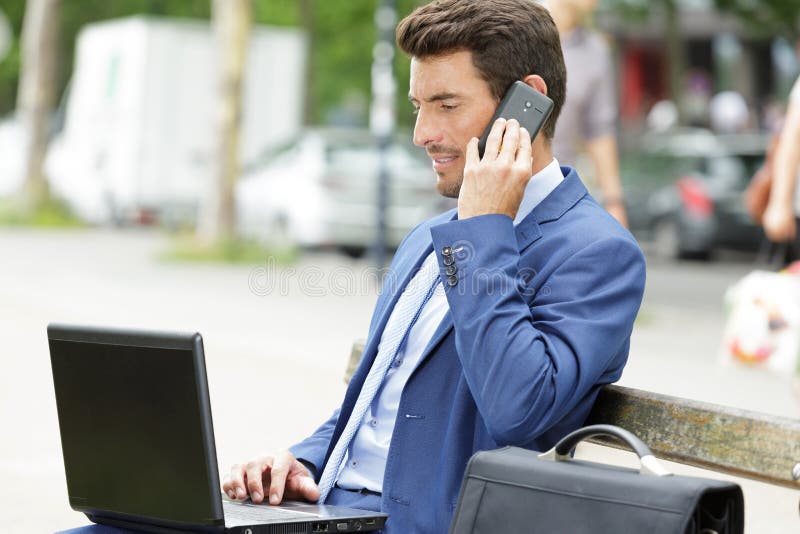 Businessman Using Laptop and Smartphone on Bench Outdoors Stock Photo ...