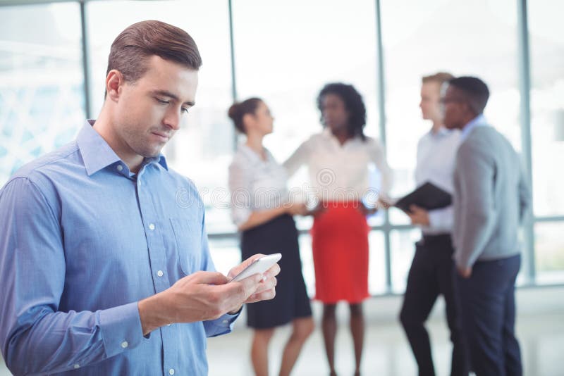 Businessman Using Mobile Phone with Colleagues Discussing in Background ...