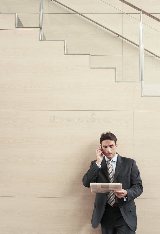 Businessman Using Mobile Phone while Reading Newspaper in Office Stock ...