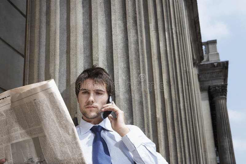 Businessman Using Mobile Phone while Reading Newspaper Stock Image ...