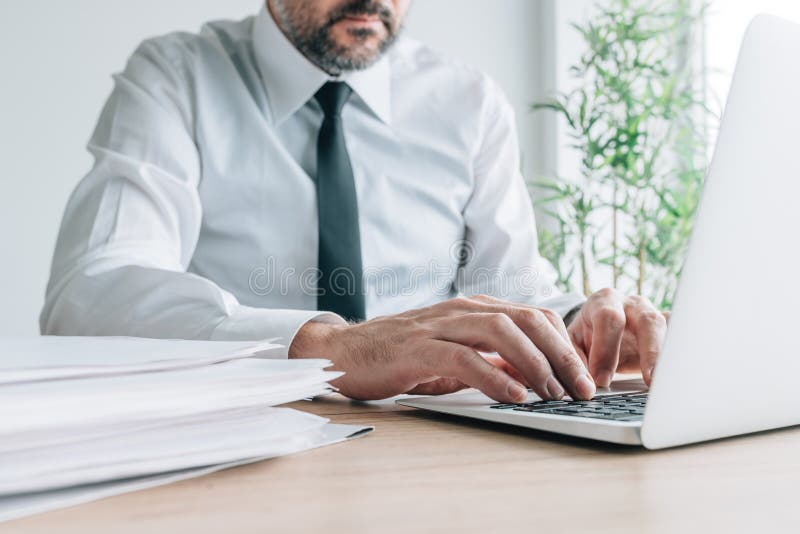 Businessman Working on Laptop Computer with Paperwork Pile on Office ...