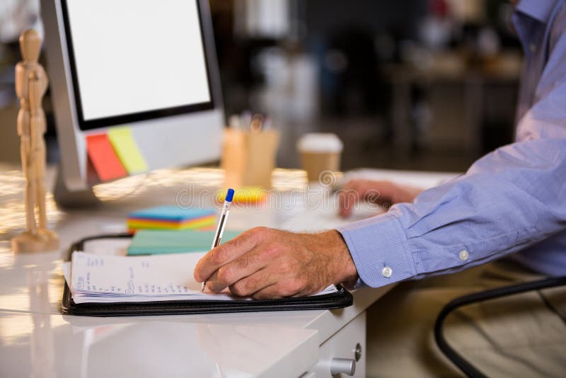 Businessman Writing on Paper at Computer Desk Stock Photo - Image of ...