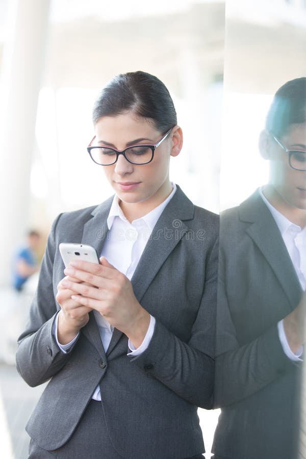 Businesswoman Using Cell Phone while Leaning on Glass Wall Stock Image ...