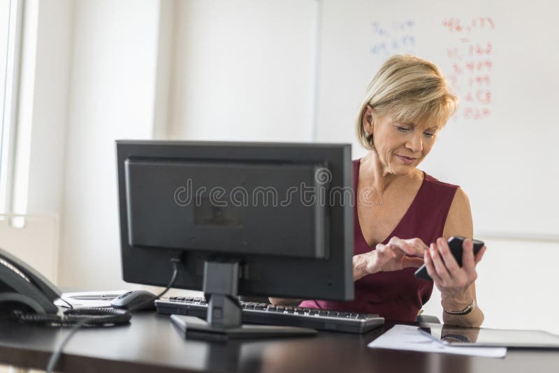 Businesswoman Using Mobile Phone at Computer Desk Stock Image - Image ...