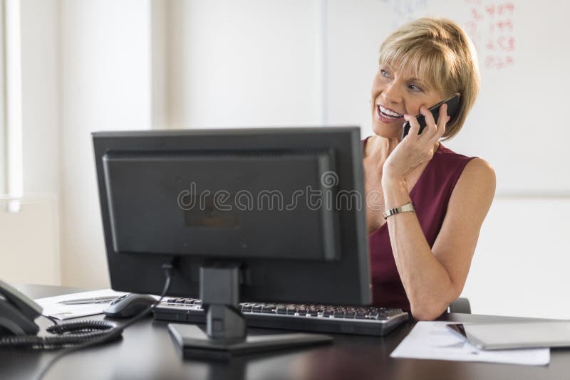 Businesswoman Using Mobile Phone at Computer Desk Stock Photo - Image ...