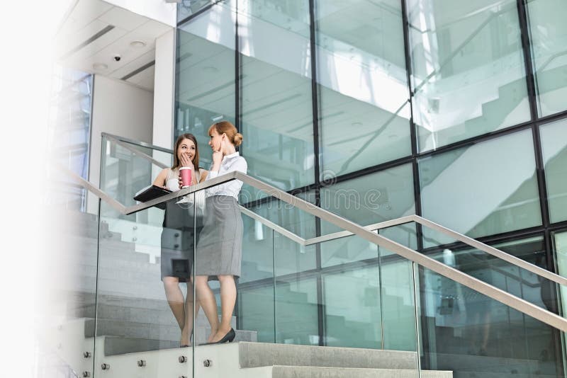 Businesswomen Conversing while Having Coffee on Steps in Office Stock ...