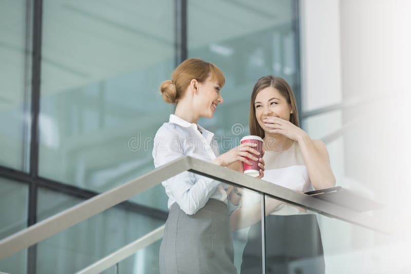 Businesswomen Gossiping while Having Coffee on Steps in Office Stock ...