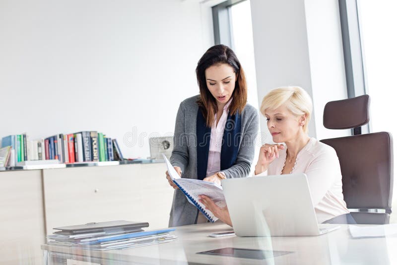 Businesswomen Reading Book at Desk in Office Stock Photo - Image of ...