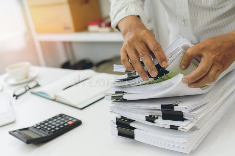 A Busy Office Worker Checking and Organizing a Large Pile of Documents ...