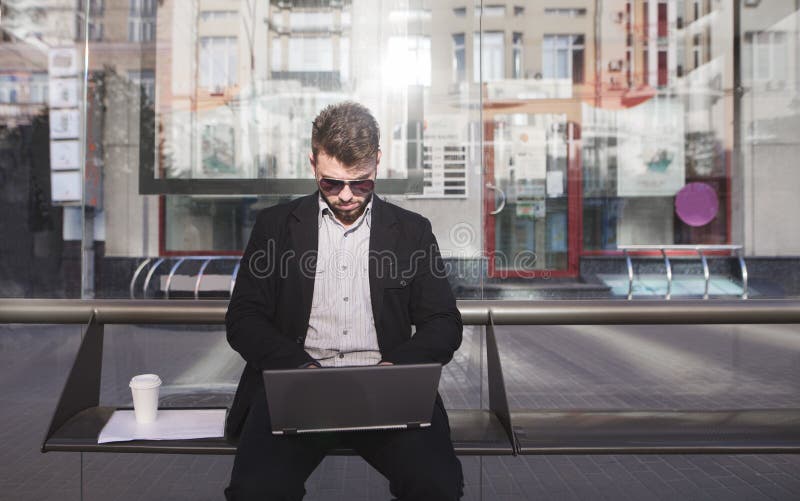Busy Office Worker Sits at a Bus Stop and Works on a Laptop. Work on ...