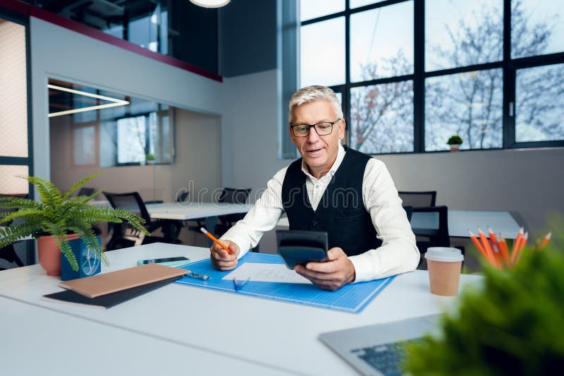 Busy Senior Man Sitting at Office Desk with Papers and Making Notes ...