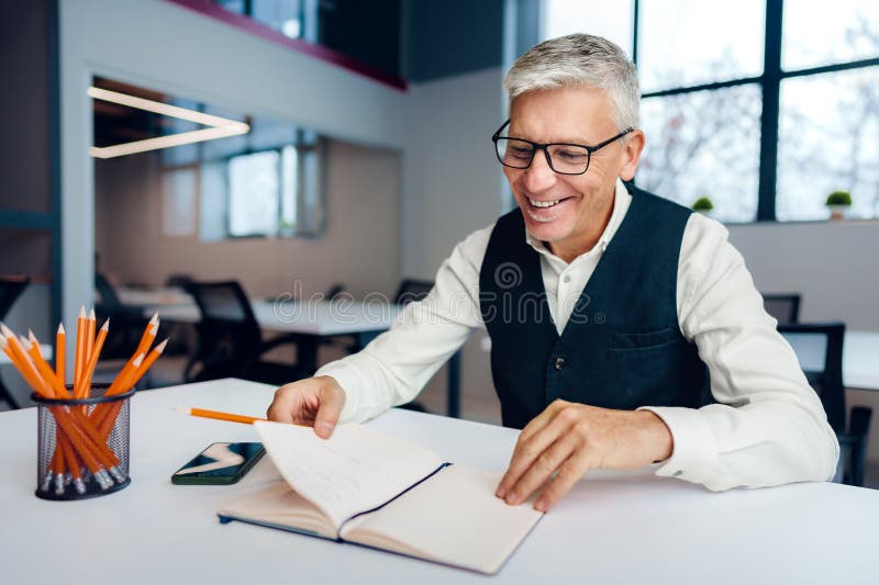 Busy Senior Man Sitting at Office Desk with Papers and Making Notes ...