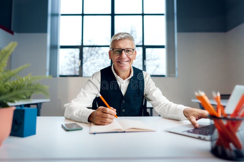 Busy Senior Man Sitting at Office Desk with Papers and Making Notes ...