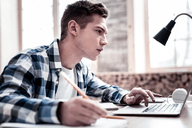 Busy Student Frowning and Looking at the Screen while Making Notes ...