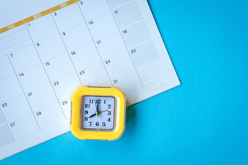 Calendar Page and Yellow Clock on Top of Blue Tabletop Stock Photo ...