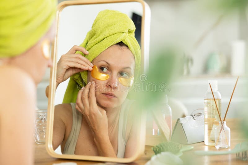 Middle-aged Woman Applying Eye Patch Mask on Her Face Sitting in Front ...