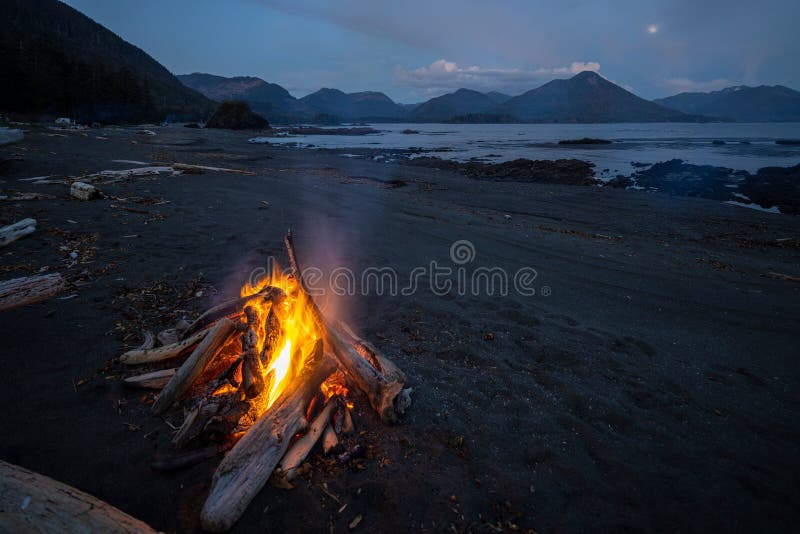Campfire on Calm Lake Shore with Mountains in the Background Stock ...