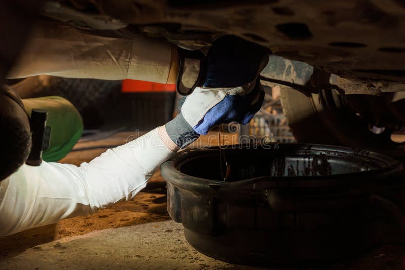 Car Mechanic Performing Oil Change Service Under Vehicle with Oil ...