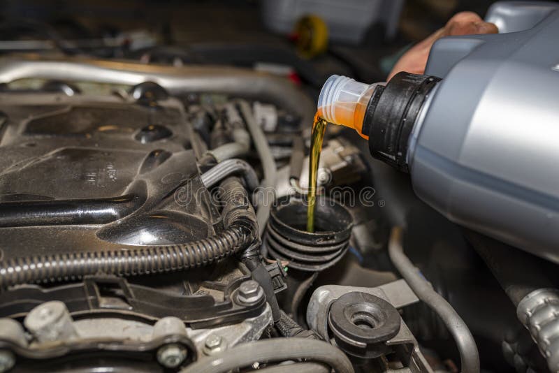 Car Mechanic Pours New Car Oil into the Engine from a Plastic Tank in a ...