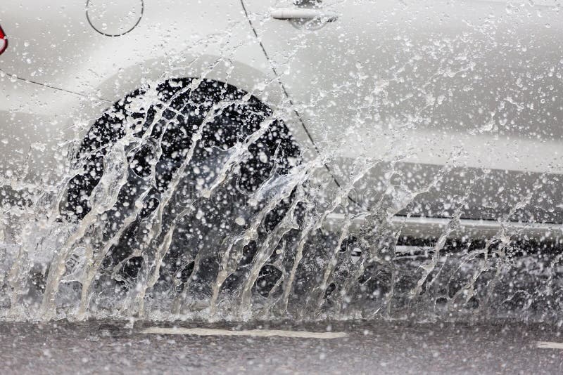 Car Motion through Big Puddle of Water Splashes from the Wheels on the ...