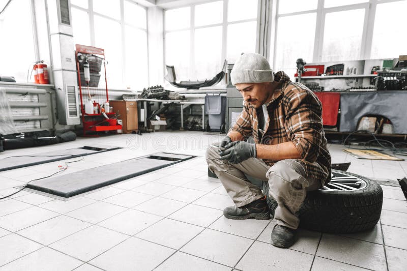 Car Service Worker Sitting on a Wheel and Resting, Using Mobile Phone ...
