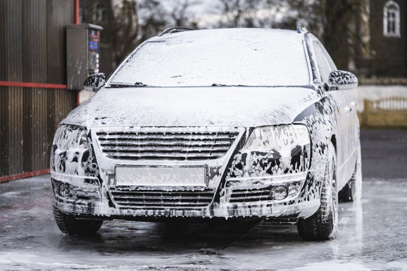 The Car at the Car Wash is Covered with Foam, Wash Under Pressure with ...