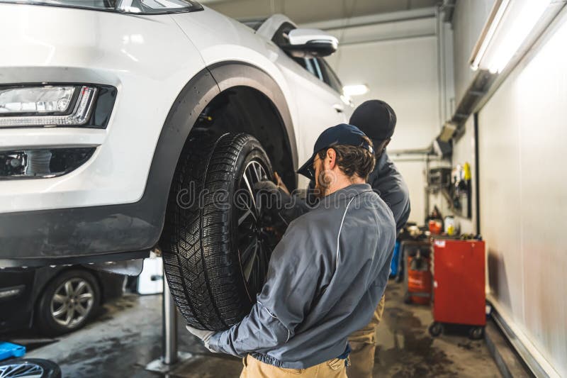 Car Wheel Changing Process in the Garage, Two Mechanics Working in the ...