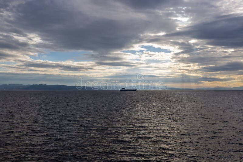 Cargo Ship on the Ocean with Dramatic Clouds, Distant Mountains, and ...