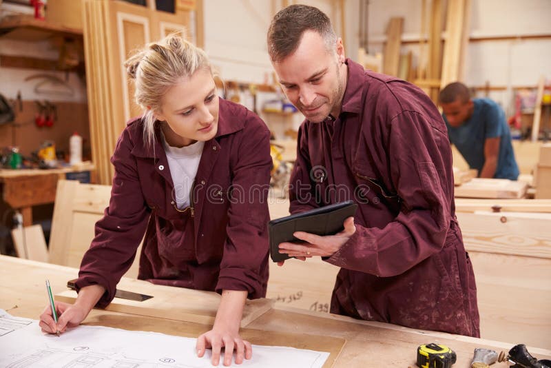 Carpenter with Apprentice Looking at Plans in Workshop Stock Photo ...