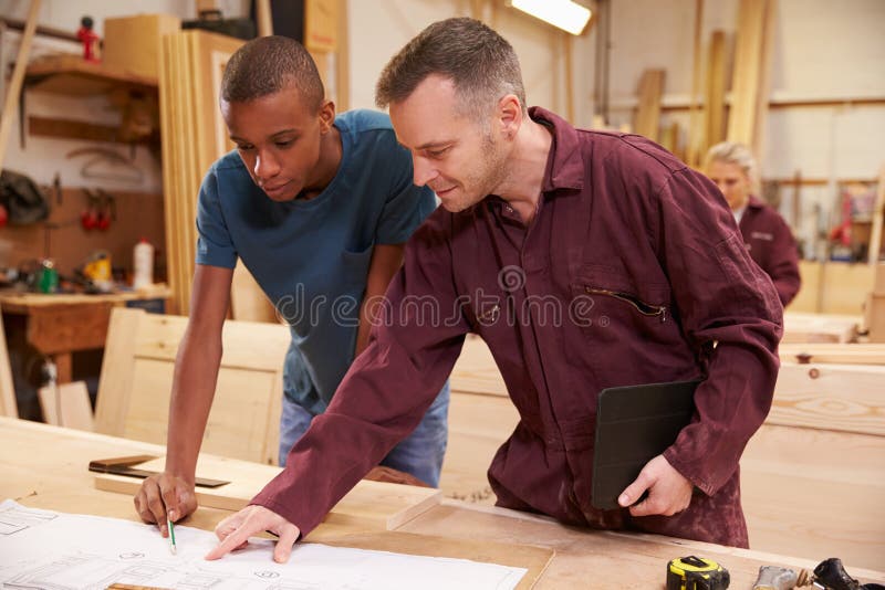Carpenter with Apprentice Looking at Plans in Workshop Stock Image ...
