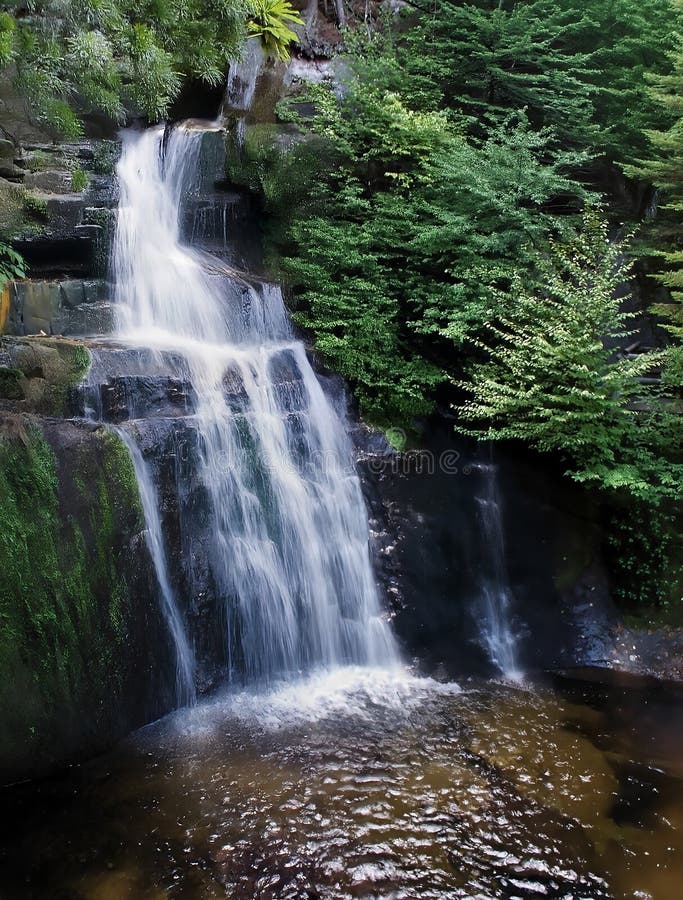 A Cascading Waterfall Flows Over Moss-covered Rocks into a Tranquil ...