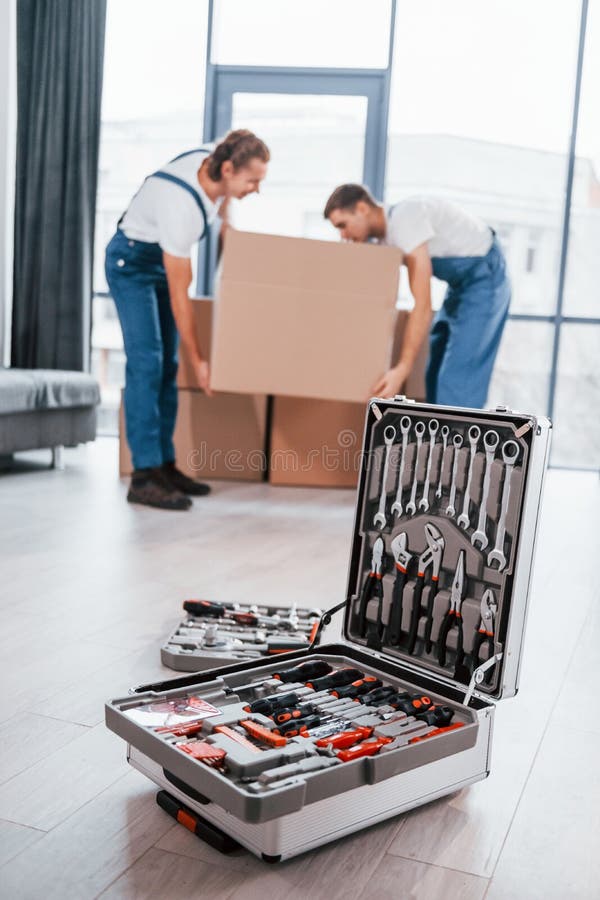 Case with Equipment. Two Young Movers in Blue Uniform Working Indoors ...