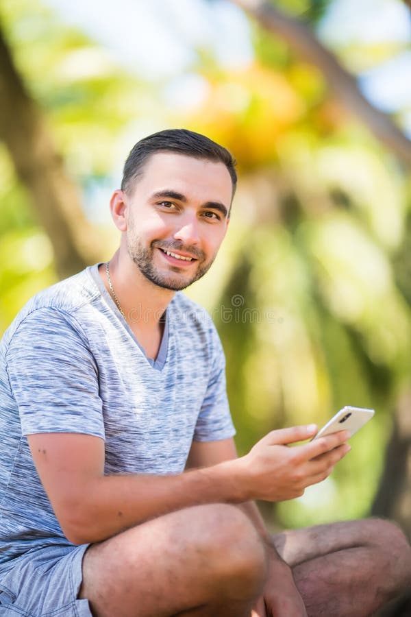 Casual Happy Man Typing on Smartphone Sitting on a Bench in a Park ...
