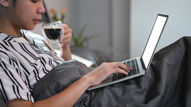 Man Drinking Hot Coffee and Using Laptop Computer on His Bed in the ...