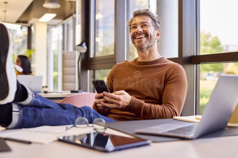 Casually Dressed Mature Businessman with Feet on Desk in Office Using ...