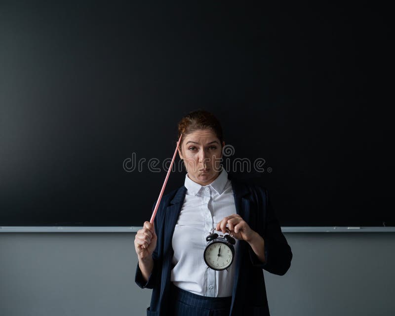 Caucasian Female Teacher In A Pantsuit Holds A Pointer And A School