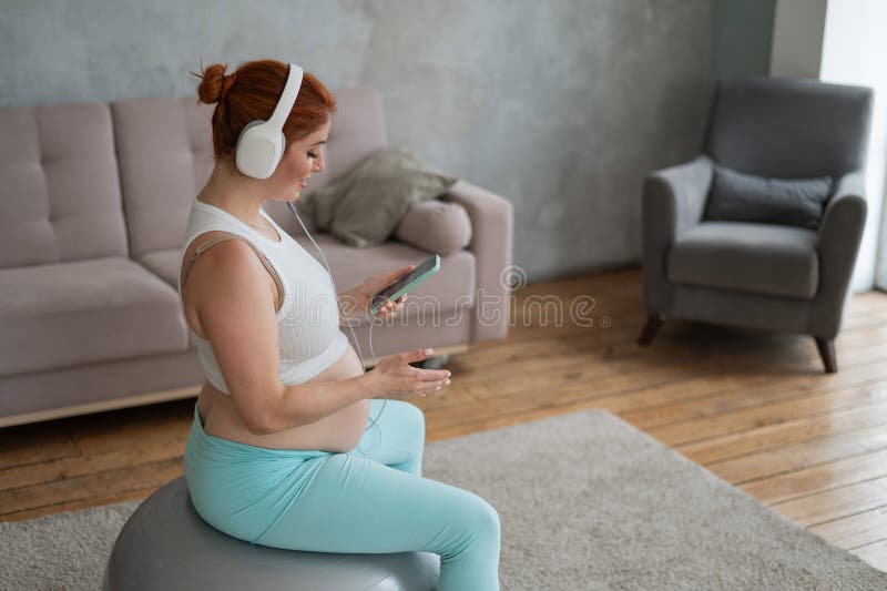 Caucasian Red Haired Pregnant Woman Sitting On Fitball And Listening To