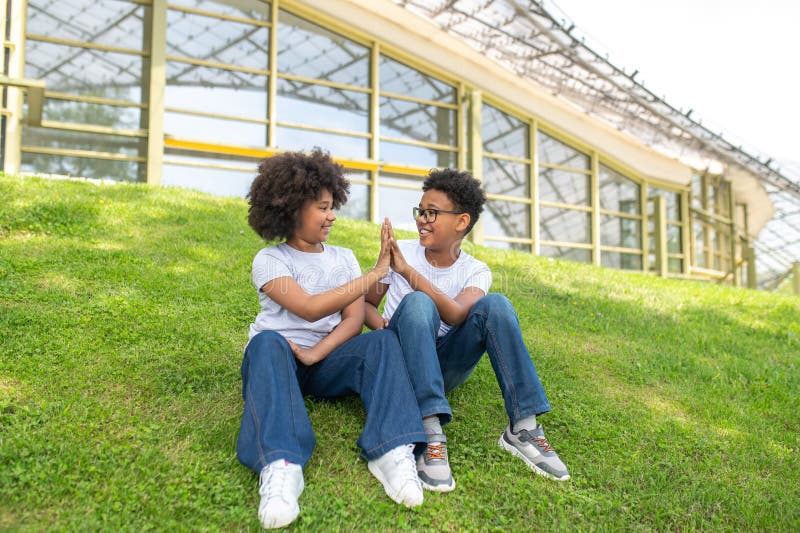 Charming Friends Sitting on Grass in Park Giving High Five. Stock Photo ...