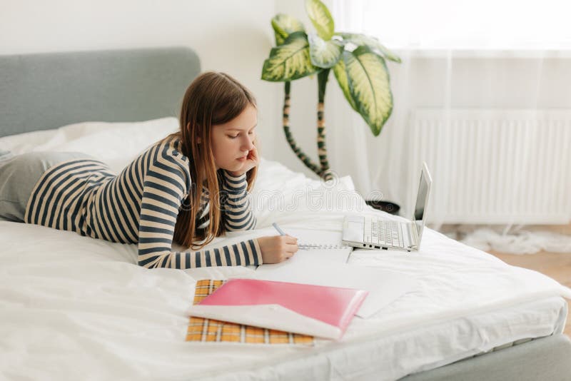 A Charming Teenage Girl is Lying on the Bed, Doing Homework with a ...