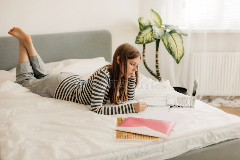 A Charming Teenage Girl is Lying on the Bed, Doing Homework with a ...