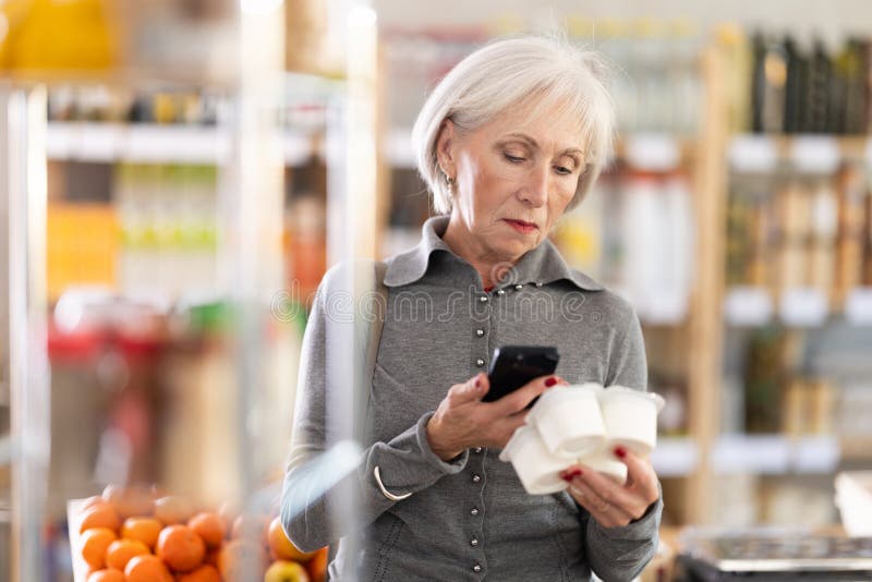 Checking Expiration Date of Yogurt - Elderly Female Shopper Scans QR Code on Label of Yogurt ...